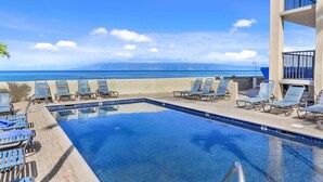 Área de piscina com espreguiçadeiras e vista para o oceano.
