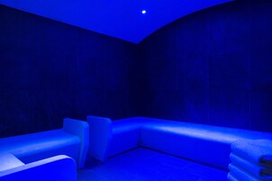 Um quarto iluminado em azul, com uma parede curva, uma área de estar e uma pilha de toalhas.