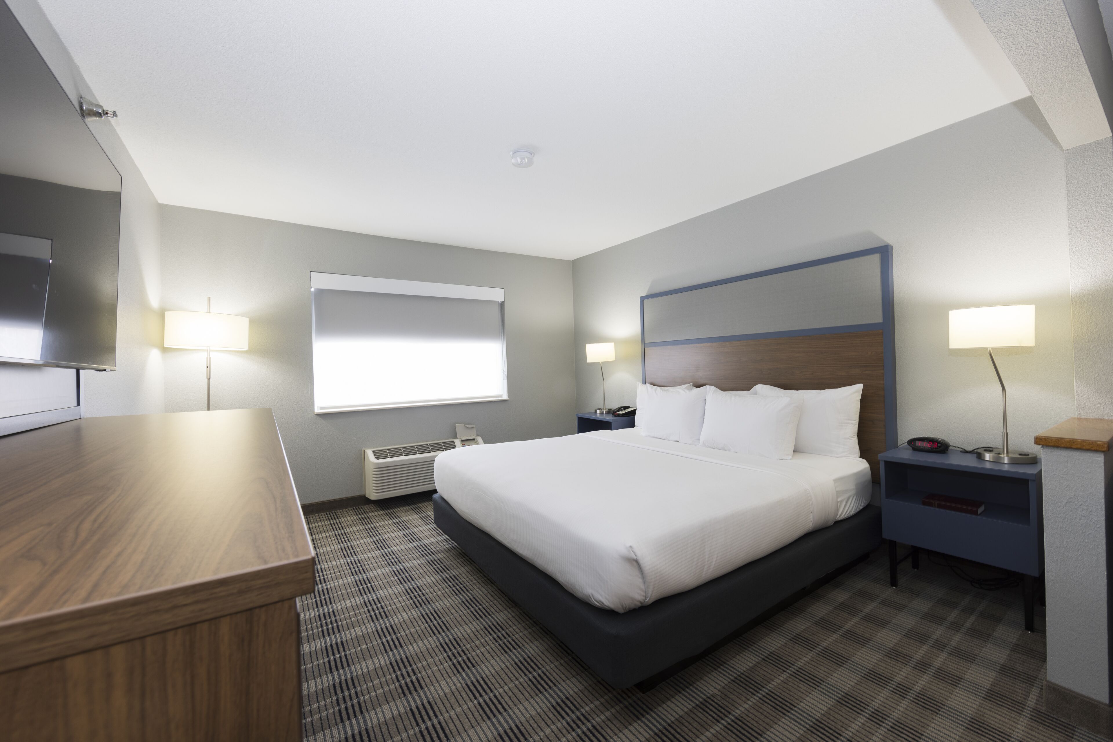Quarto de hotel com uma cama grande, mesas de cabeceira, uma escrivaninha e uma janela.