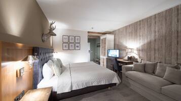 Quarto de hotel moderno com uma cama grande, um sofá, uma escrivaninha com um computador e um chifre de veado fixado na parede.