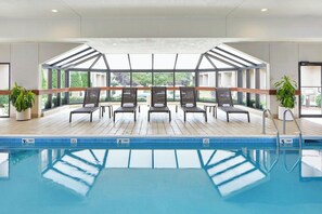 Uma piscina com espreguiçadeiras, teto de vidro e plantas em vasos.