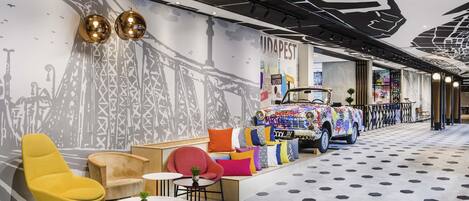 Decoração moderna com um mural, espaço para sentar e exposição de carros antigos.
