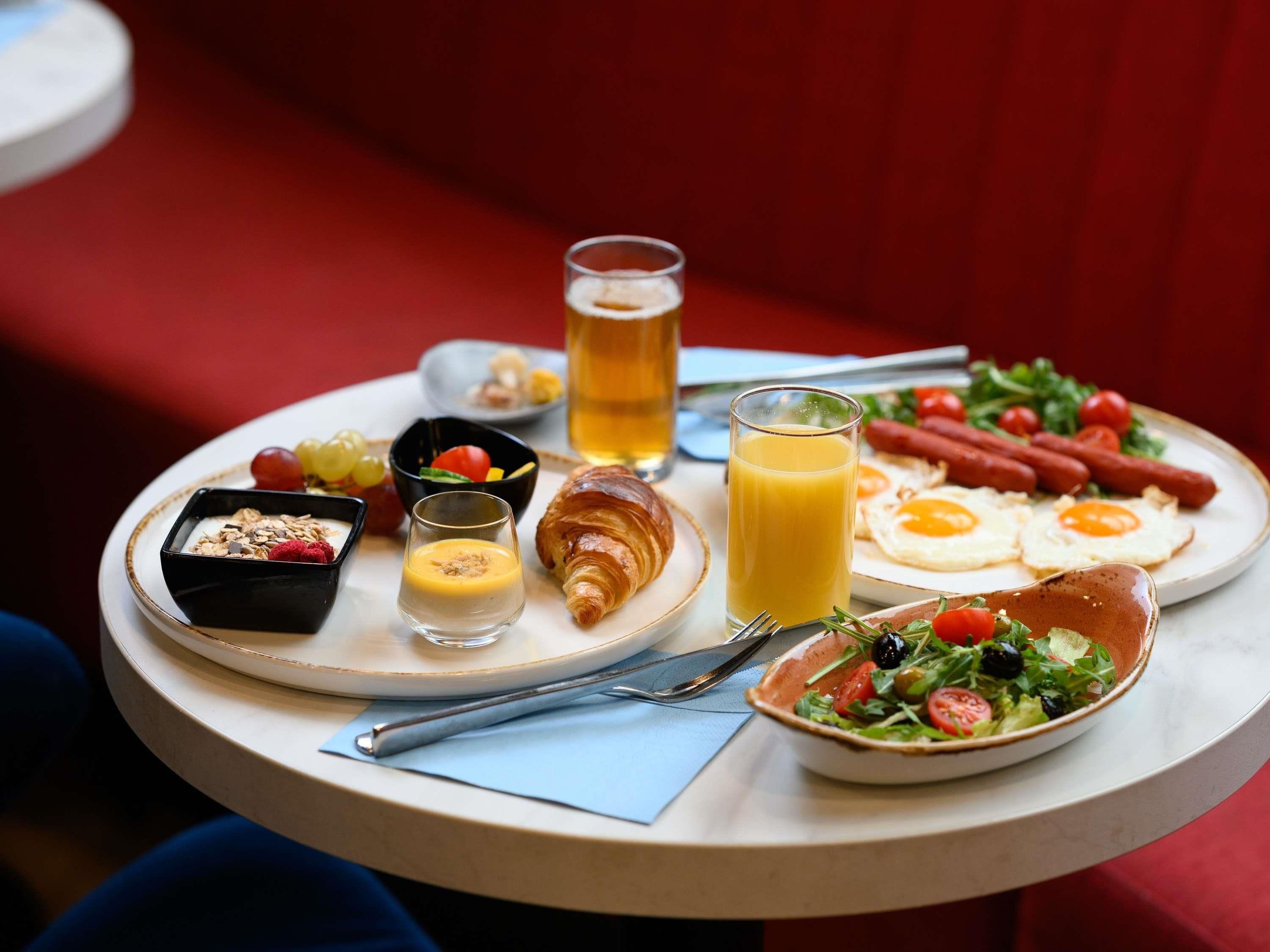 Uma bandeja de café da manhã com croissants, ovos, salsichas, salada e um copo de suco de laranja.