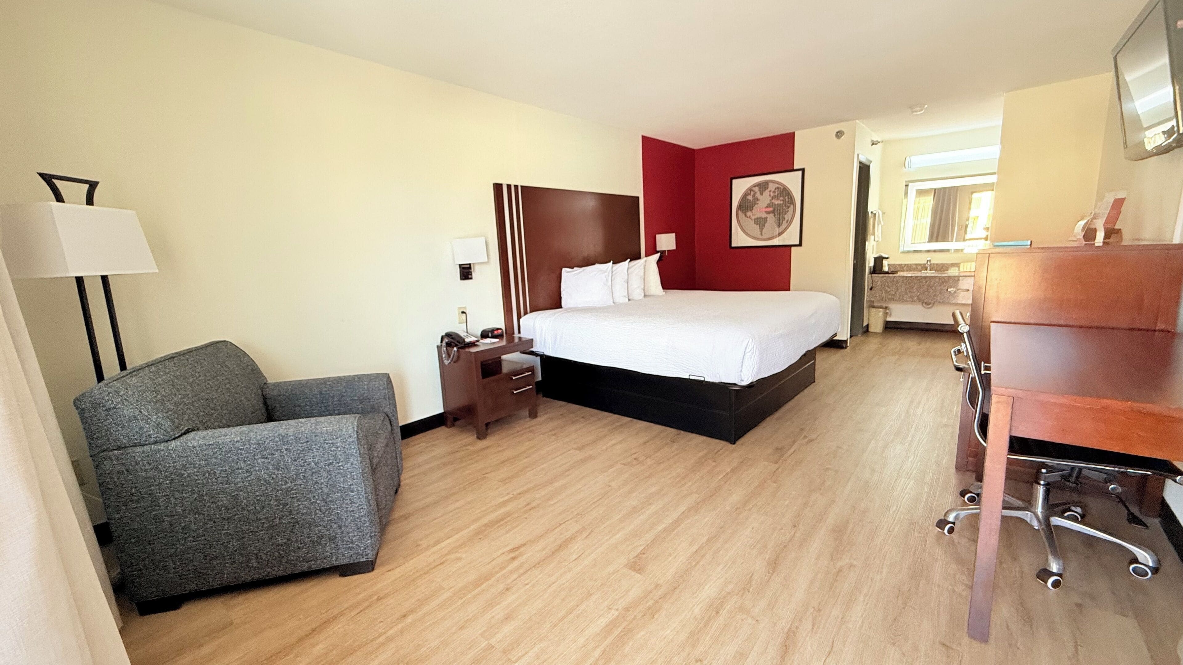 Quarto de hotel com uma cama, escrivaninha, cadeira, cômoda e banheiro.