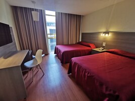 Quarto de hotel com duas camas, uma mesa, uma cadeira e uma janela com cortinas.