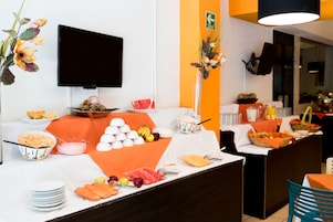 Disposição de buffet com diversos alimentos e uma televisão fixada na parede.