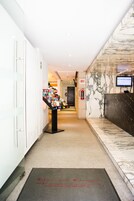 Um saguão de hotel com balcão de recepção, uma seleção de revistas e uma parede de mármore.