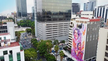 Vista urbana com edifícios modernos, rua movimentada e um grande mural em um prédio.