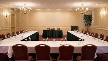 Uma sala de conferências com uma mesa comprida, cadeiras vermelhas e toalha de mesa verde.
