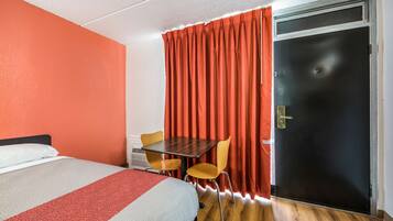 Quarto de hotel com cama, mesa, duas cadeiras e uma porta.