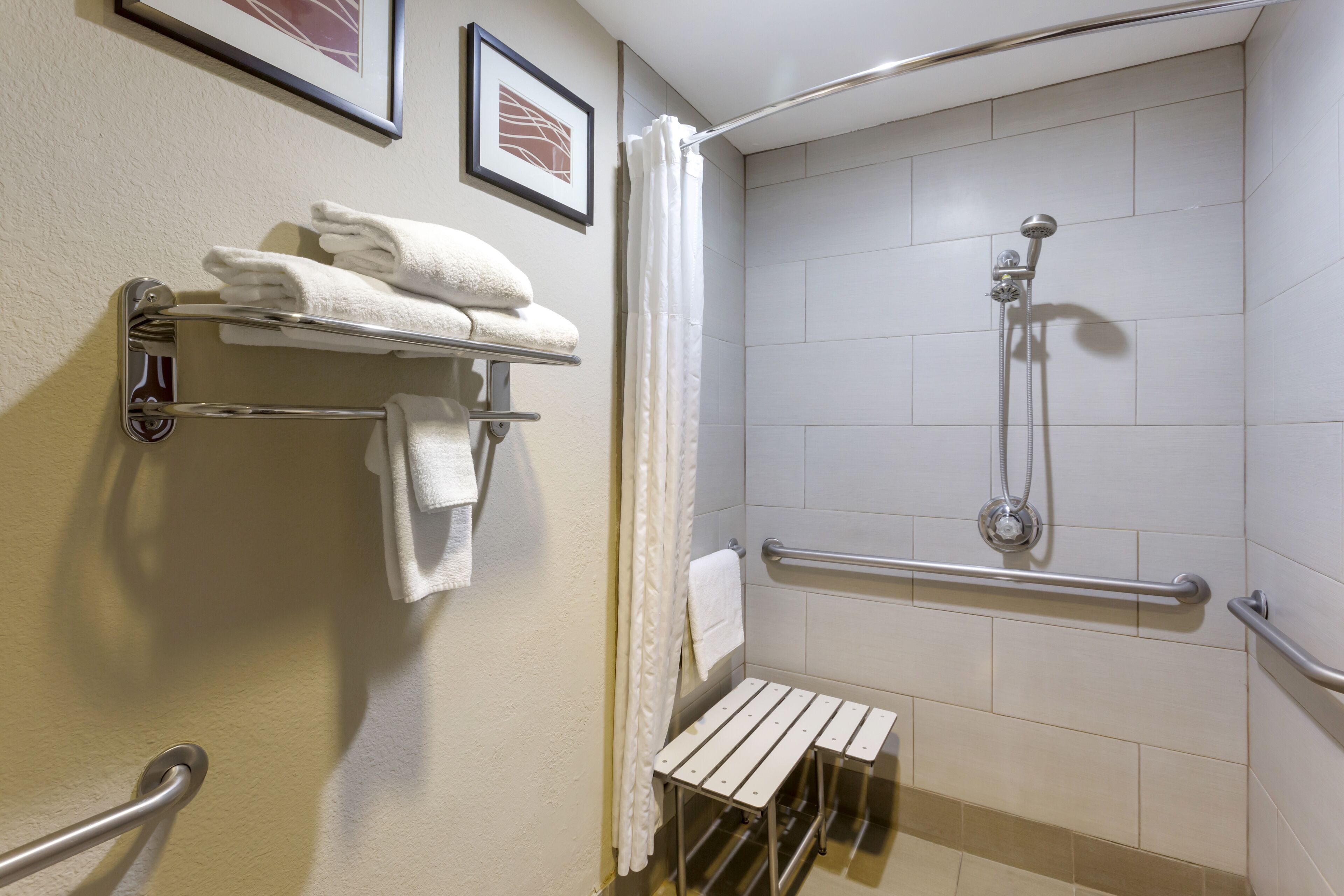 Área de duche com barra de apoio, toalheiro branco e chuveiro.