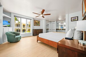 Quarto de hotel com cama, poltrona, ventilador de teto, televisão, pintura e vista para o exterior.