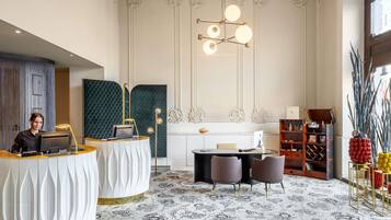 Um saguão de hotel com balcão de atendimento, área de estar e uma estante de livros.