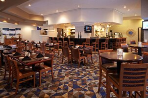 Um restaurante com várias mesas e cadeiras, um chão estampado e um bar com uma televisão.