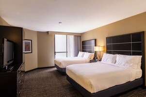 Quarto de hotel com duas camas, televisão, secretária e janela com cortinas.