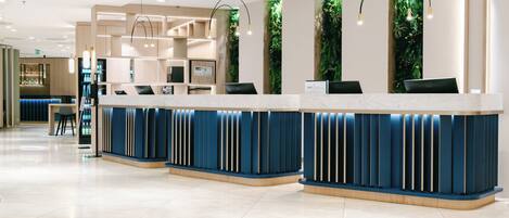 Uma área de recepção moderna com balcão de mármore, decoração azul e bege, e detalhes de vegetação vertical.
