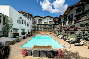 Piscina com espreguiçadeiras e guarda-sóis, rodeada por edifícios altos com varandas.
