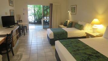 Quarto de hotel com duas camas, uma escrivaninha com televisão e vista para um jardim por uma porta de correr.