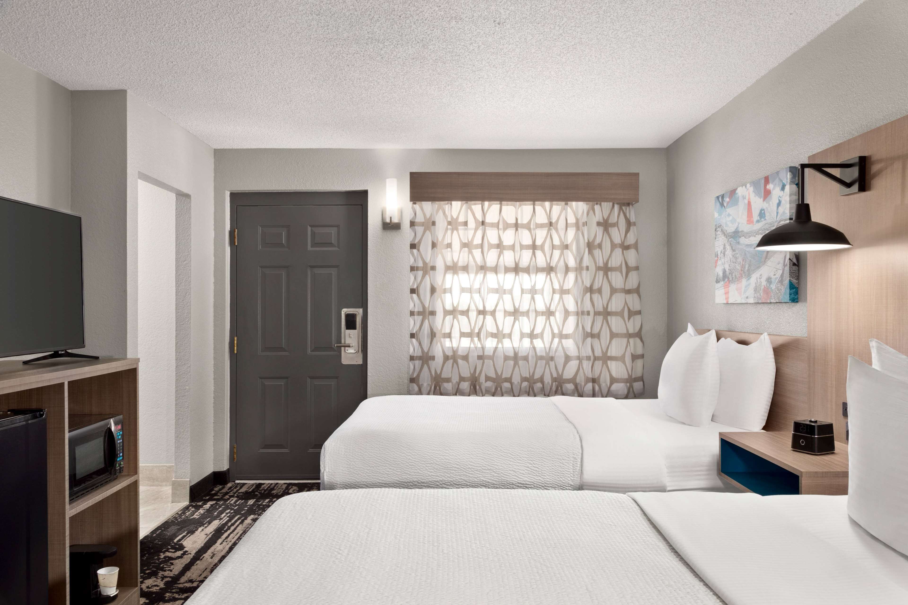Quarto de hotel com duas camas, televisão, micro-ondas e cortina estampada.