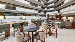 Um hall de hotel moderno com várias áreas de refeições, diferentes arranjos de assentos e um espaço amplo central.