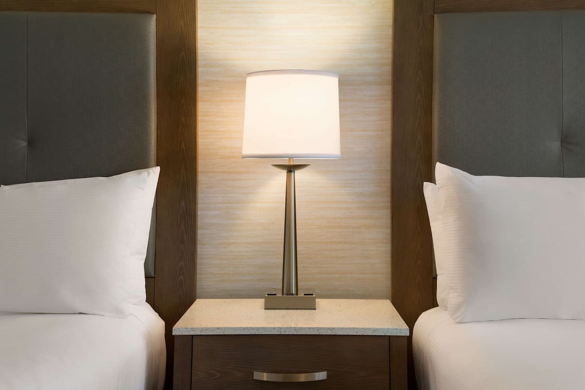 Cama bem arrumada com travesseiro branco e mesa de cabeceira com abajur.