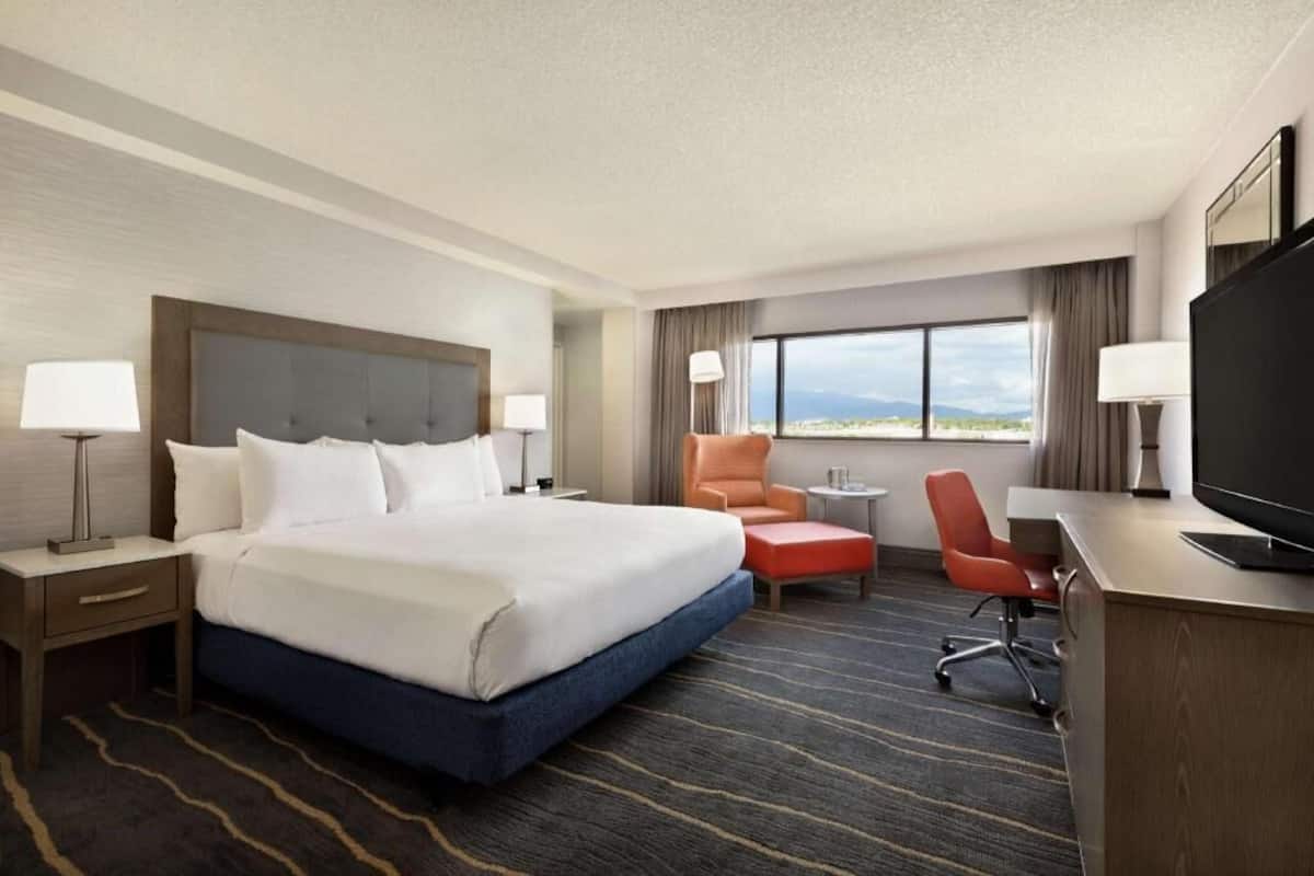 Quarto de hotel com uma cama grande, uma escrivaninha, televisão e vista para o exterior.