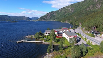 Um hotel com fachada em vermelho e branco, localizado às margens de um lago com um cais, rodeado por vegetação e montanhas.