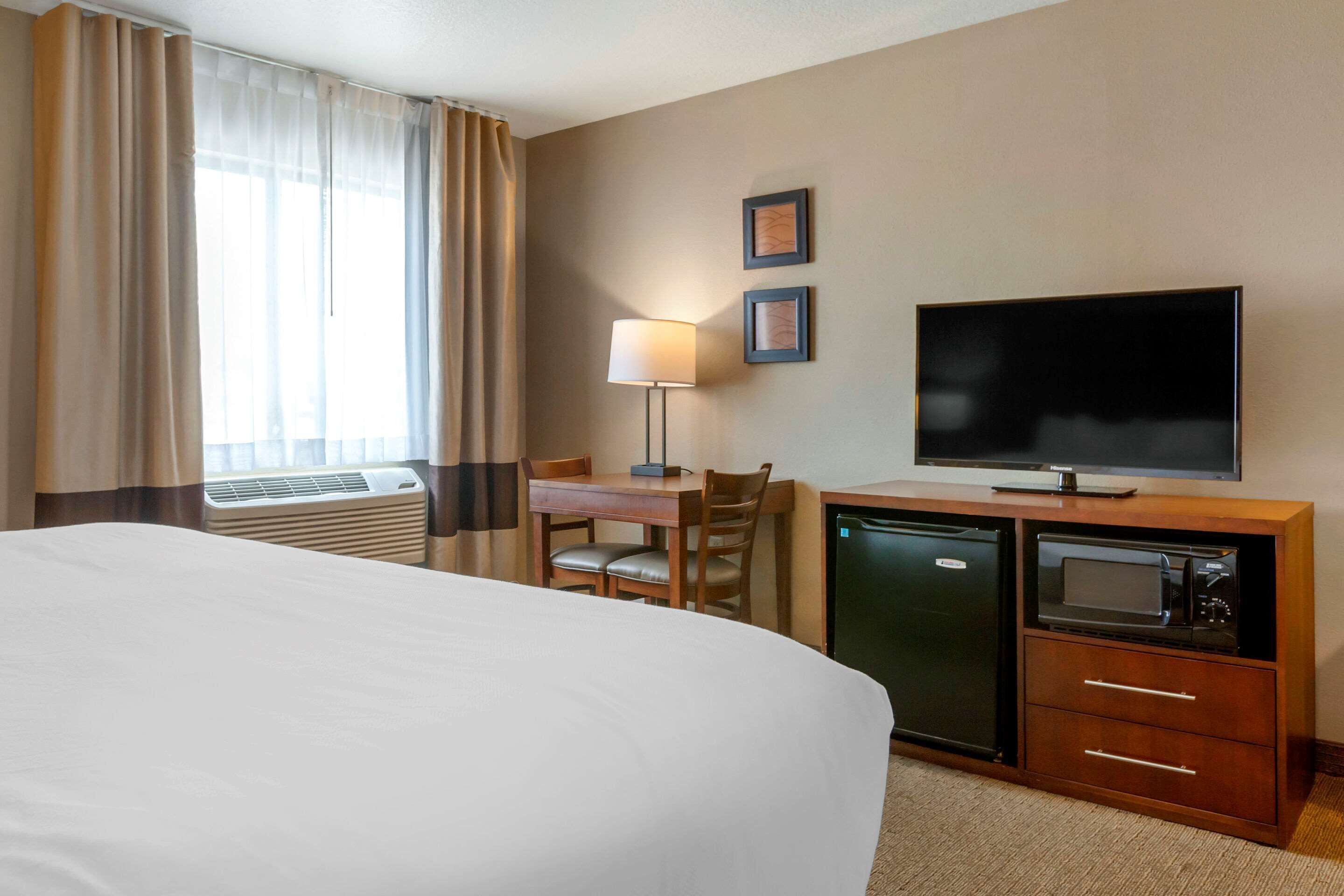 Quarto de hotel com uma cama grande, uma escrivaninha com abajur, televisão, micro-ondas e ar condicionado.