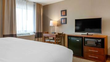 Quarto de hotel com uma cama grande, uma escrivaninha com abajur, televisão, micro-ondas e ar condicionado.