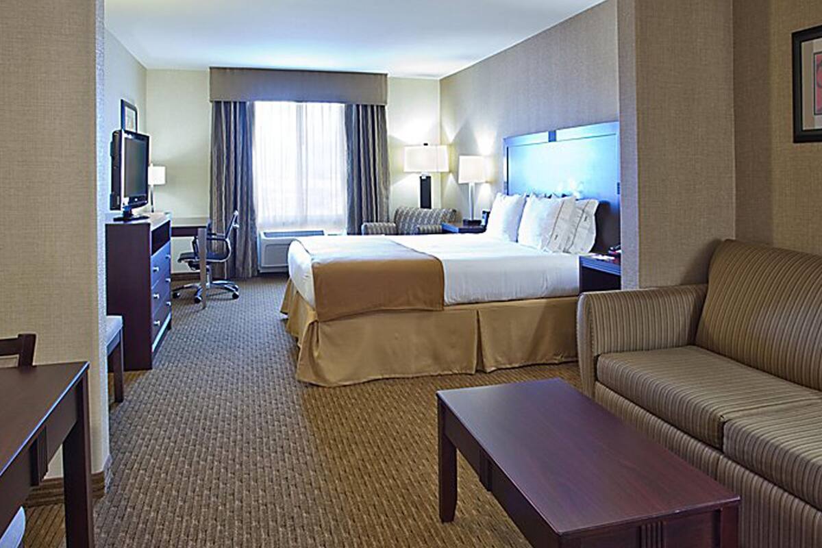 Quarto de hotel com cama, sofá, escrivaninha, televisão e janela com cortinas.