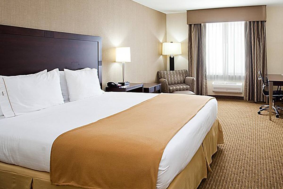Quarto de hotel com uma cama grande, uma escrivaninha, uma cadeira e uma luminária.