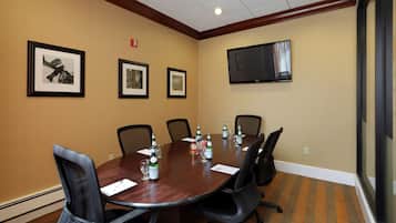 Uma sala de conferências com uma mesa de madeira, seis cadeiras e uma televisão de tela plana na parede.