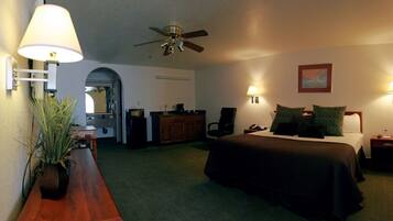 Quarto de hotel com cama, luminárias de cabeceira, escrivaninha com luminária, ventoinha no teto, micro-ondas, cafeteira, cadeira e mesa pequena.