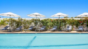 Piscina com espreguiçadeiras e guarda-sóis, cercada por um muro coberto de plantas trepadeiras e flores.