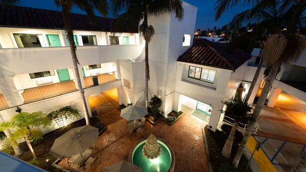 Hotel com vários andares e um pátio central com uma fonte, área de estar ao ar livre e palmeiras.