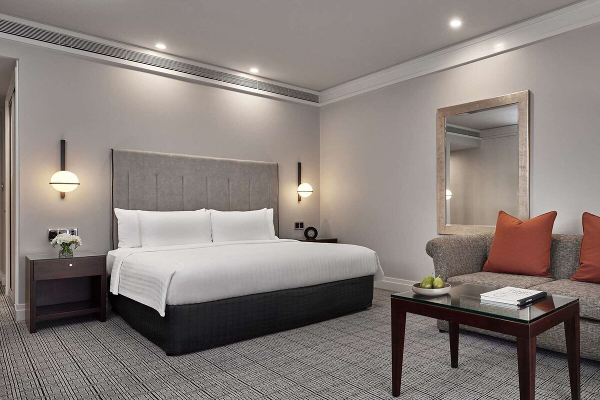 Quarto de hotel com cama, mesas de cabeceira, sofá, mesa de centro e espelho.