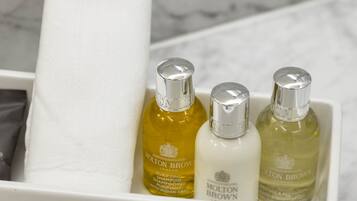 Caixa de higiene branca com três frascos de shampoo e condicionador Molton Brown, e uma toalha branca.