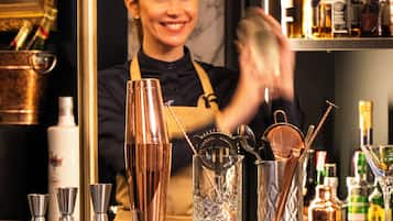 Uma área de bar com um barman, diversas ferramentas de bar e garrafas de bebidas alcoólicas.