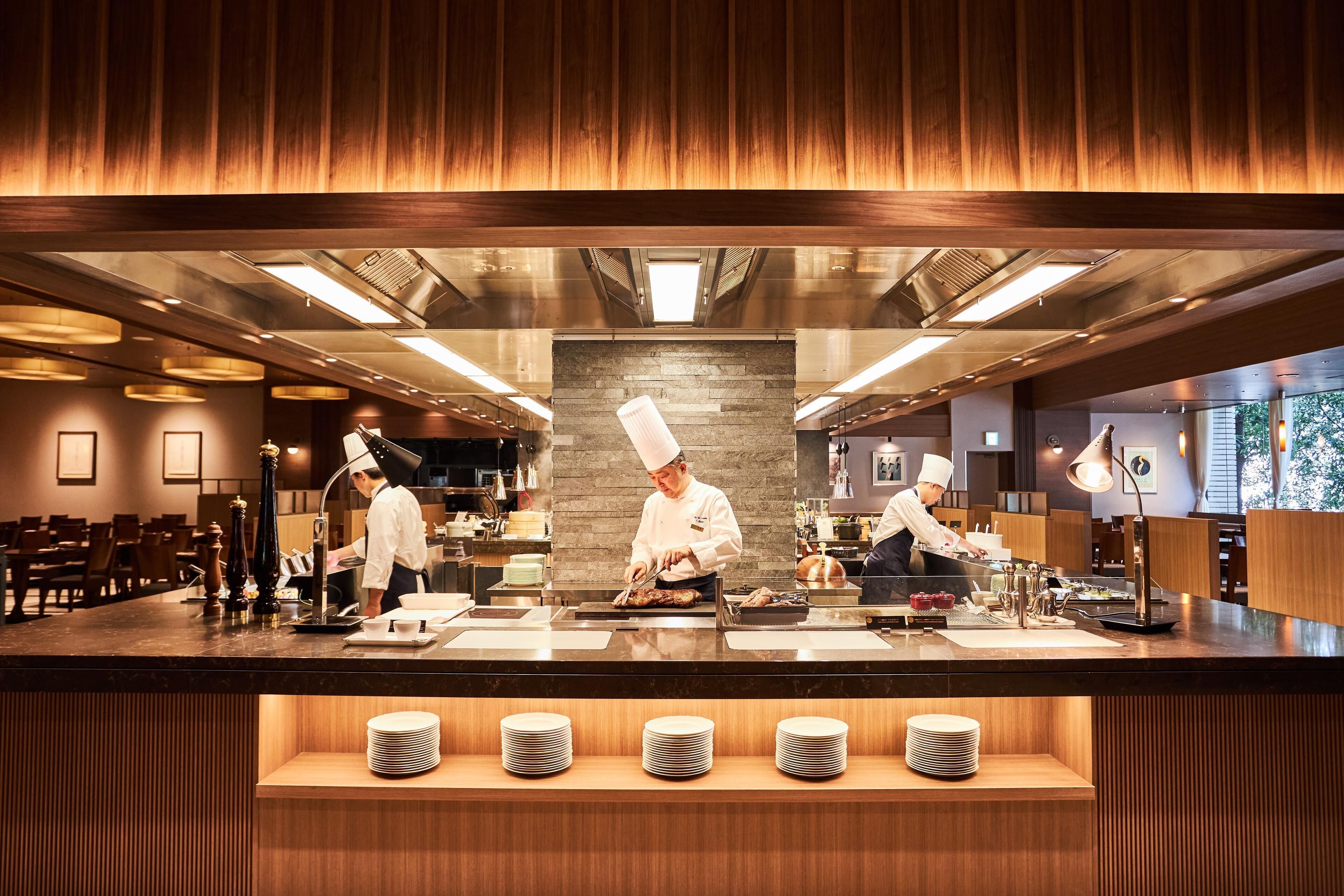 Cozinha de restaurante com chefs preparando comida, painéis de madeira e design moderno.