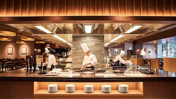 Cozinha de restaurante com chefs preparando comida, painéis de madeira e design moderno.