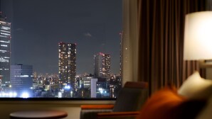 Quarto de hotel com vista para a paisagem urbana noturna, apresentando edifícios altos e o horizonte da cidade.