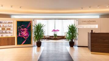 Um lobby de hotel moderno com balcão de recepção, uma grande pintura abstrata e plantas em vasos.