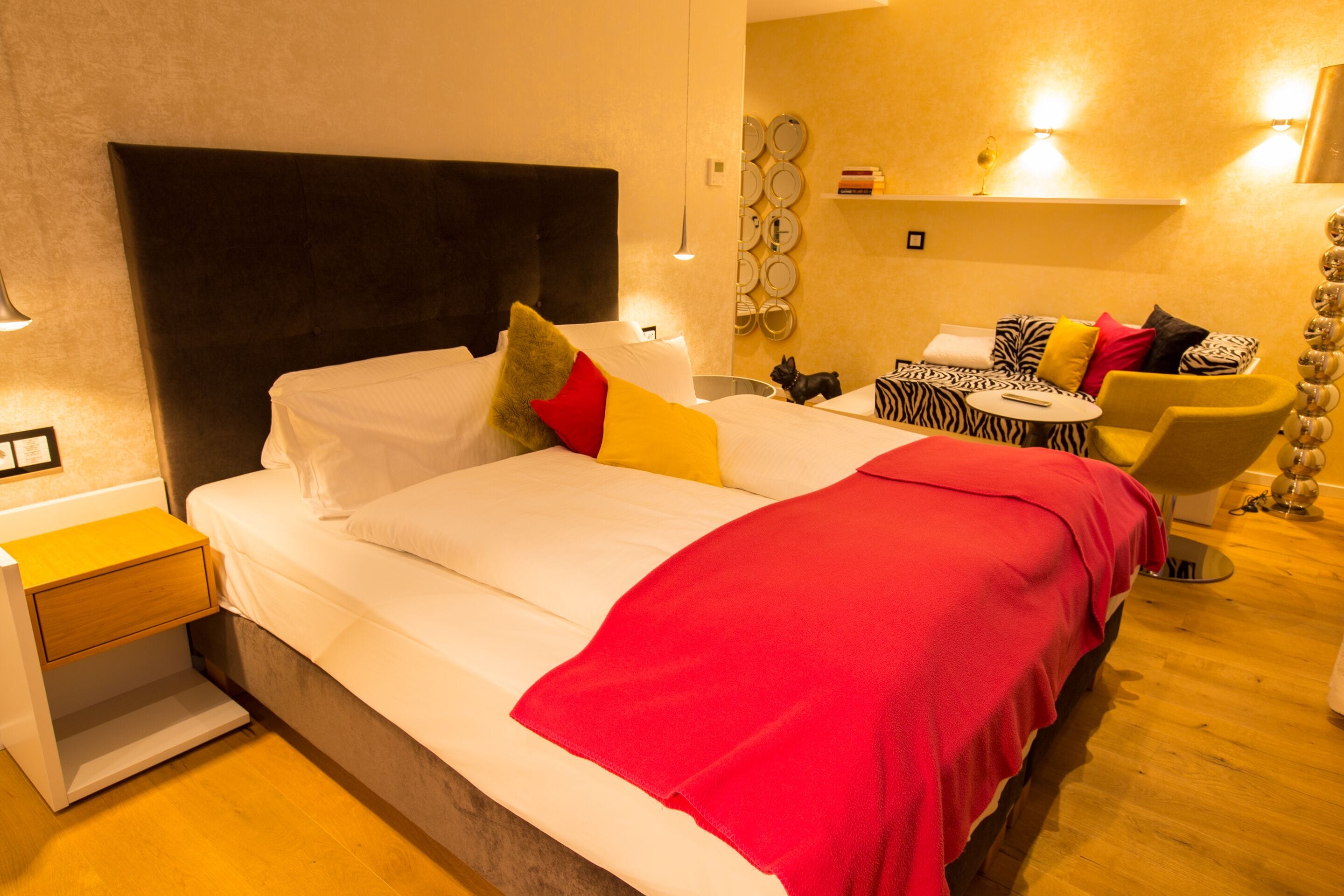 Quarto de hotel com uma cama grande, uma mesinha de cabeceira, uma cadeira e uma pequena mesa com abajur.