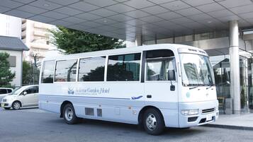 Um ônibus branco com a inscrição 'Bellflower Garden Hotel' e 'Aeroporto Internacional de Kansai' estacionado em frente a um edifício.