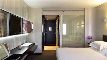 Quarto de hotel com cama, escrivaninha com laptop, televisão e porta que dá para outro cômodo.