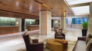 Um lobby moderno com balcão de recepção, assentos de couro, uma mesa de centro e uma grande planta em vaso.