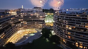 Um hotel moderno com vários sacadões, um pátio central e vista para fogos de artifício ao fundo.