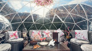 Um espaço de estar acolhedor com estrutura em cúpula de vidro, mobiliário de vime e almofadas florais.