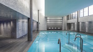 Piscina interior com água cristalina, rodeada por paredes de tijolo modernas e grandes janelas que permitem a entrada de luz natural.