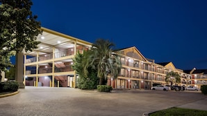 Um hotel com vários andares, varandas, estacionamento e palmeiras.